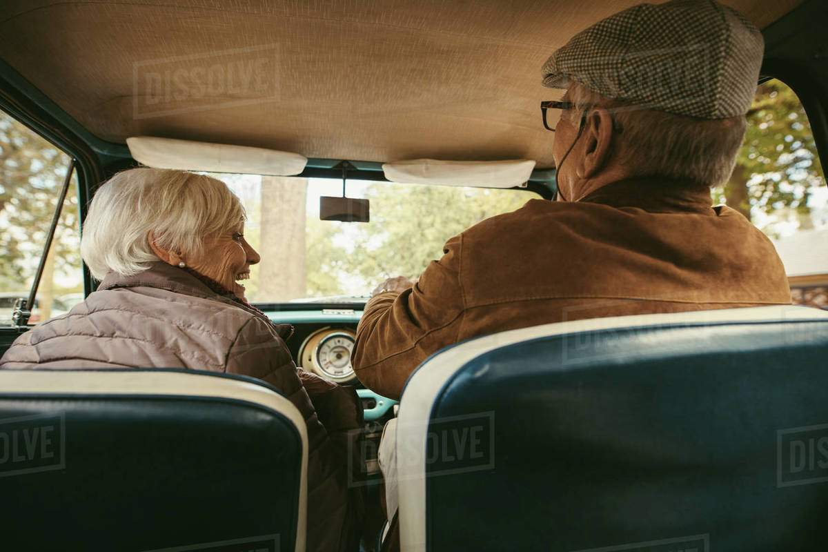 Rear view of old couple driving a car. Senior man wearing hat driving ...