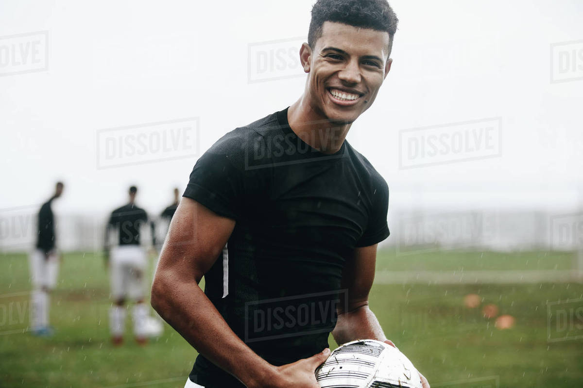 Portrait of a smiling footballer standing on field in rain. Cheerful ...