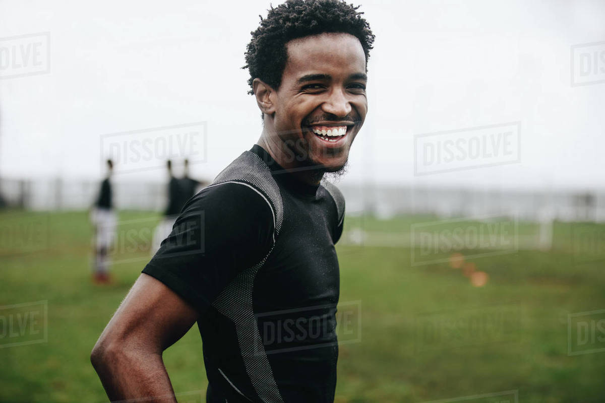 Portrait of a cheerful footballer standing on field during practice ...