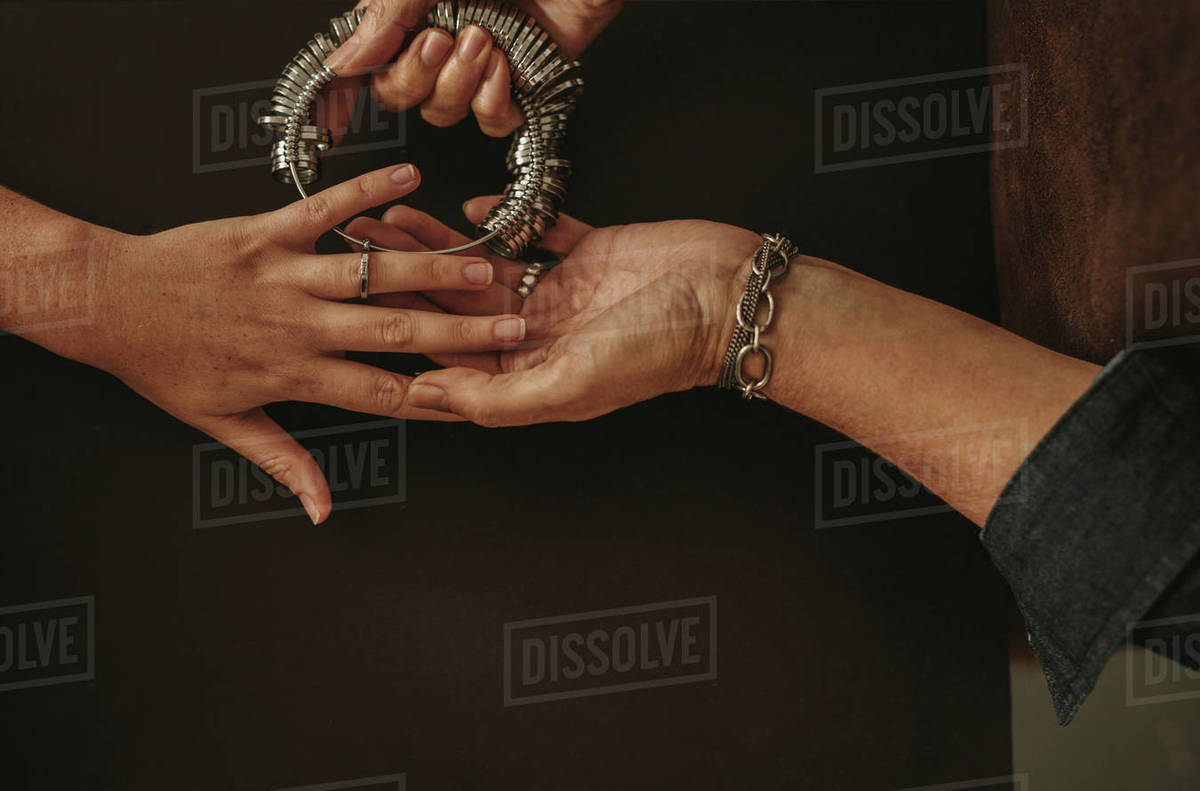 Closeup of woman checking ring size of female hand in jewelry shop ...