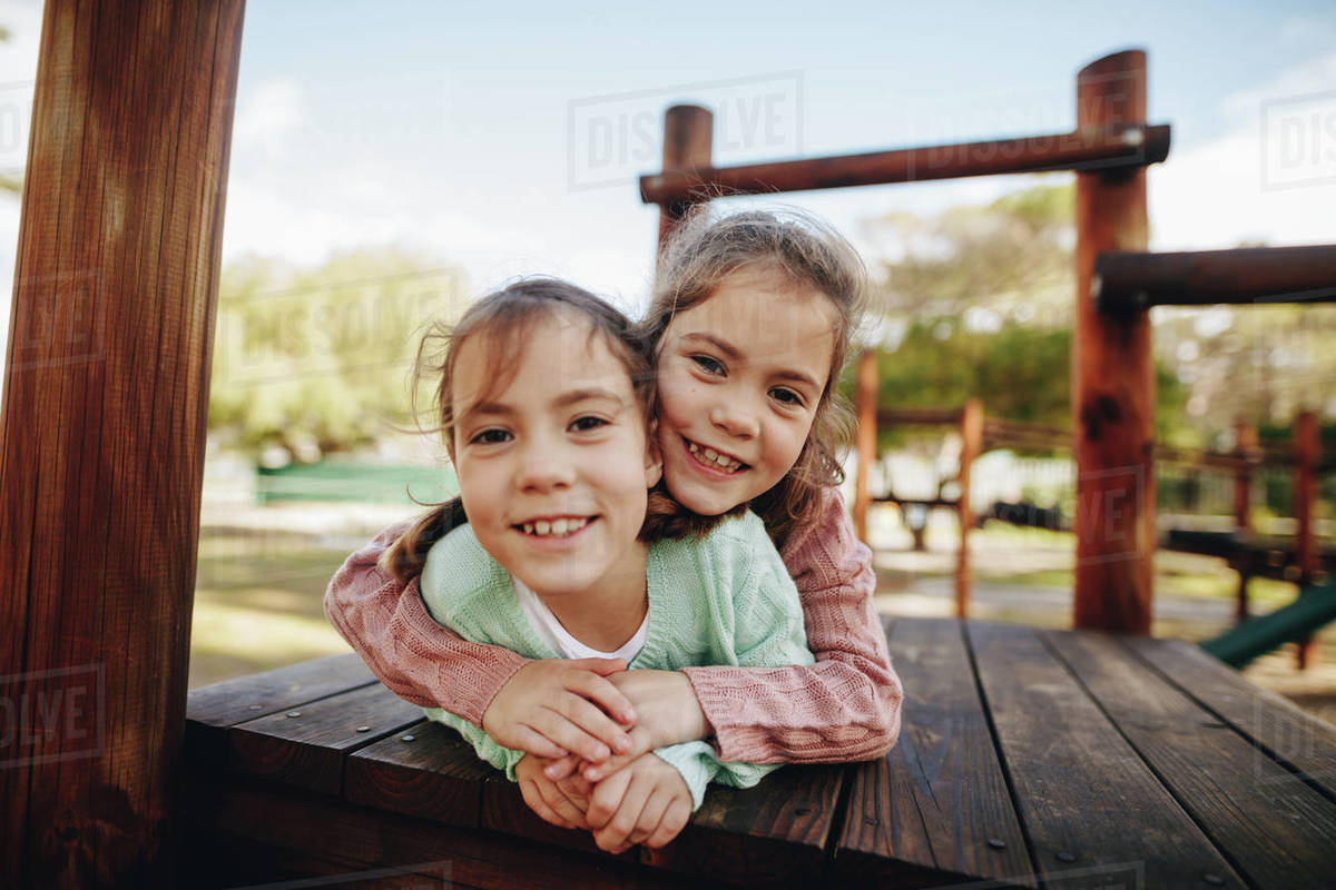 Little girl hugging her twin sister while lying in a wooden structure ...