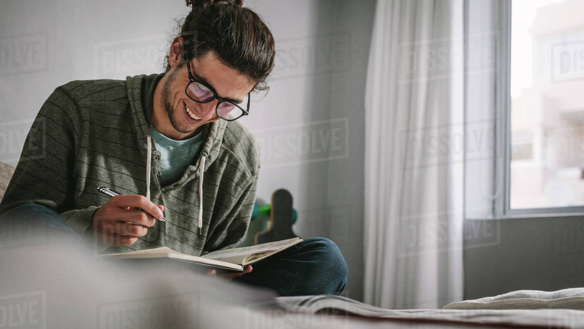 Cheerful young man preparing notes and studying sitting at home beside ...