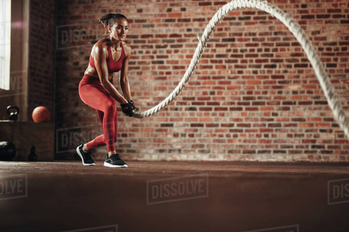 Woman using training rope for exercise at gym. Athlete working out with ...