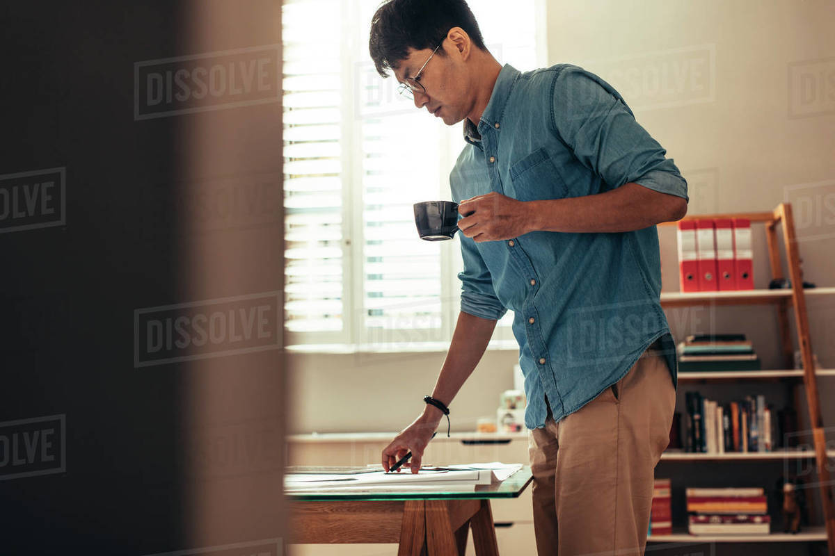 Man with coffee standing at table looking at building plan. Architect ...