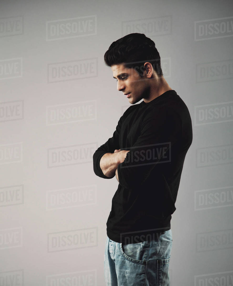 Young man in casuals standing with arms crossed looking down. Male ...