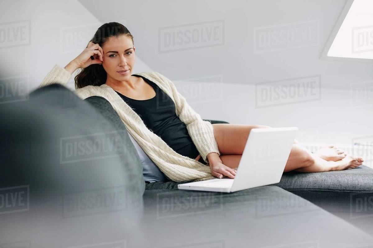 Portrait of attractive young woman with a laptop sitting on a couch ...