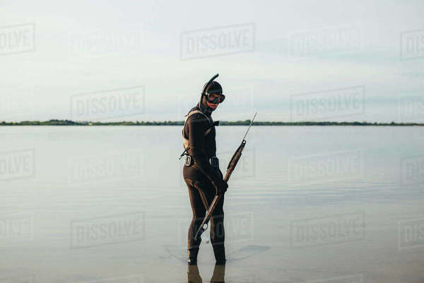 Rear view of spear fisherman standing in sea water looking over ...