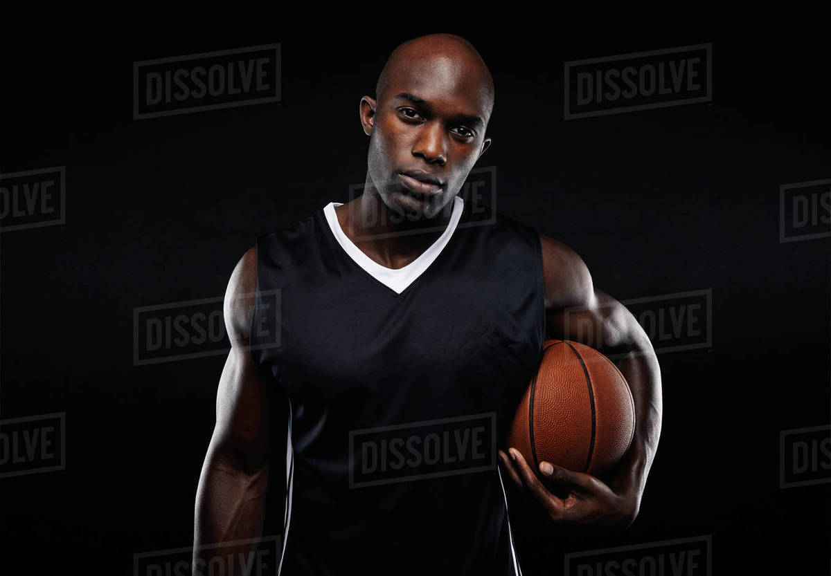 Portrait of confident young man with strong build holding a basket ball ...