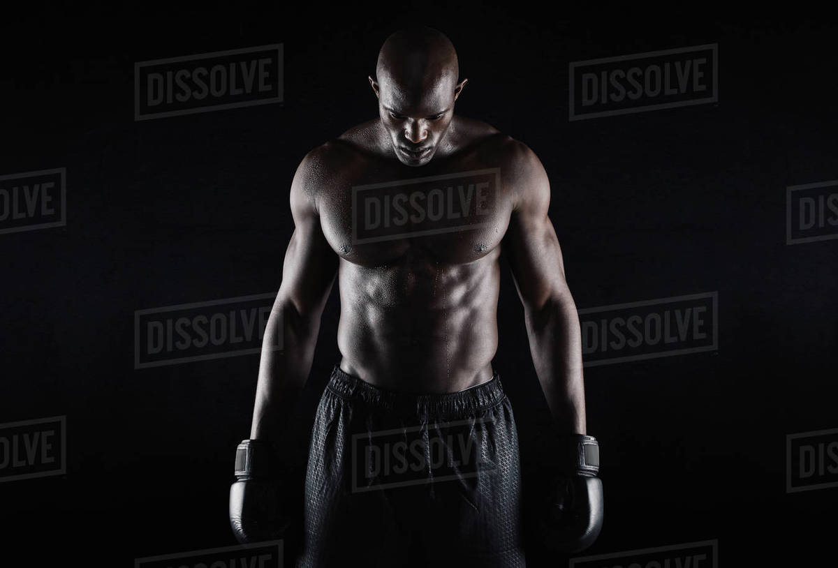 Portrait of fit young man wearing boxing gloves looking down on black ...