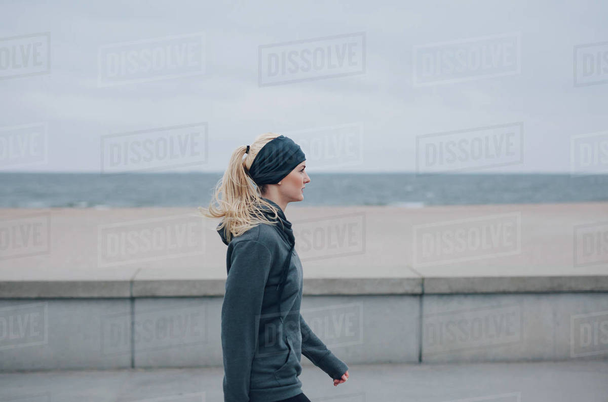Side view of confident fit young woman walking on the sea front road in ...