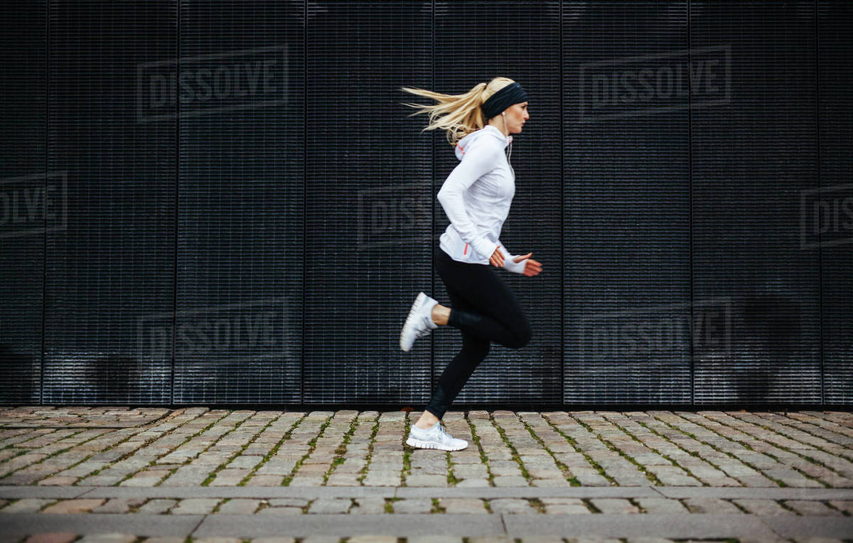Side view of sporty young woman running on sidewalk in morning. Health ...