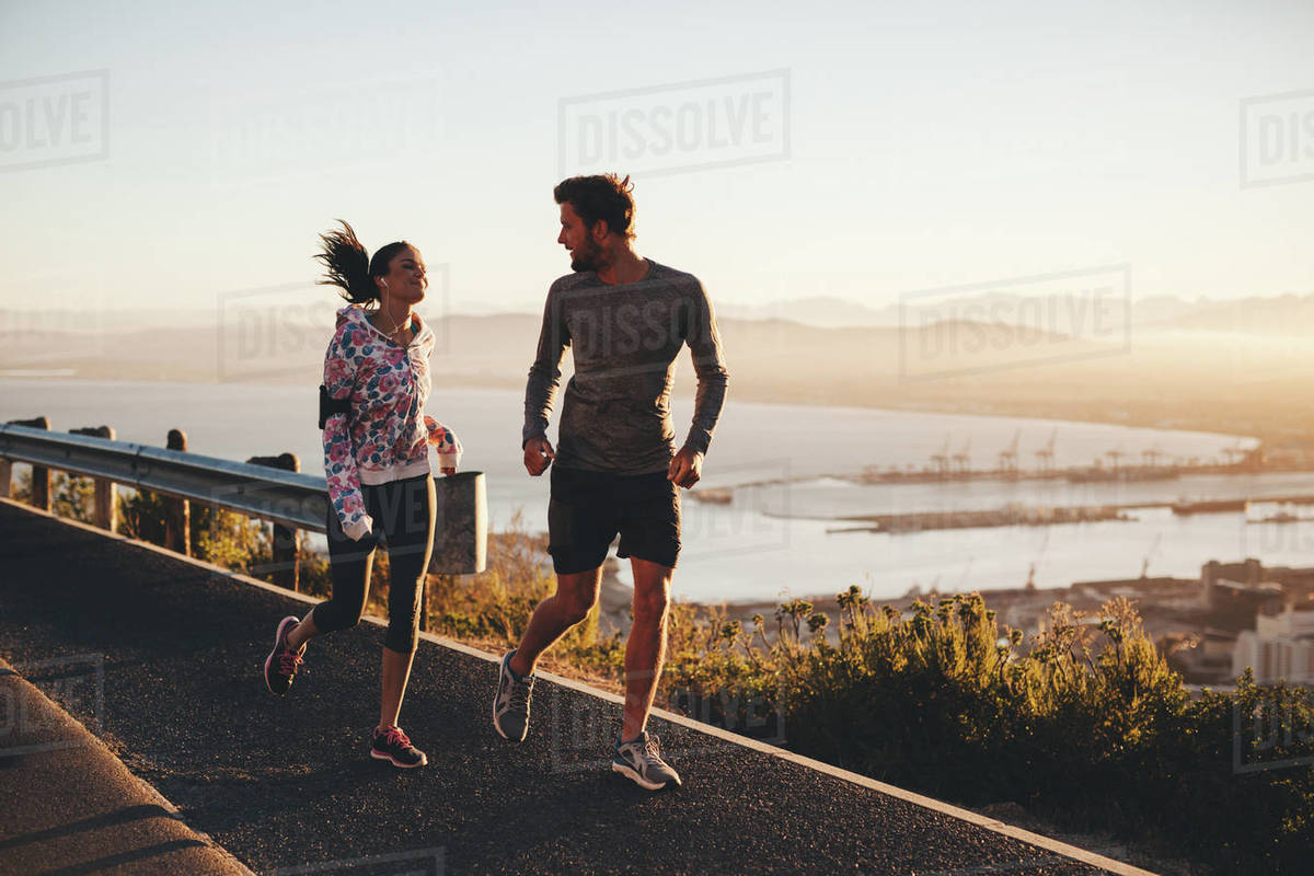 Shot of two people running on a country road in morning. Young man and ...