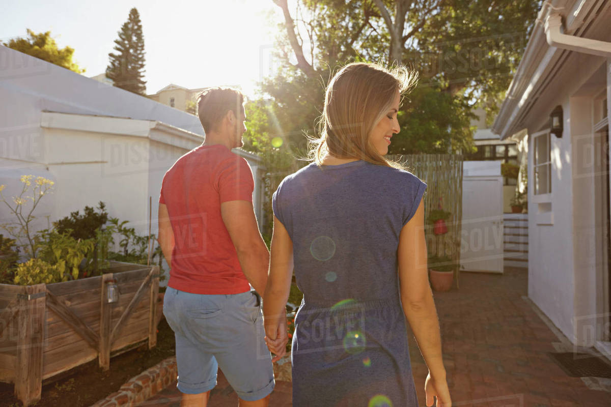 Rear view of young couple walking towards their house. Couple in ...
