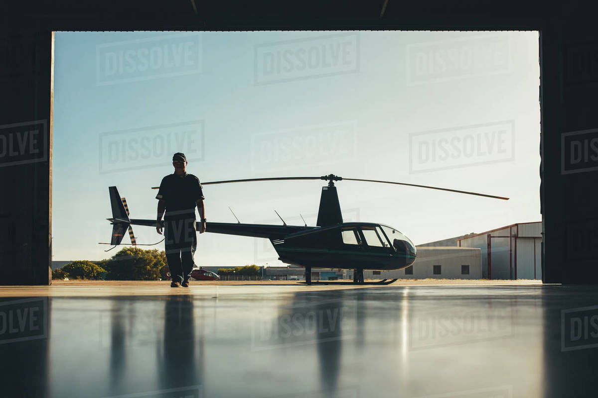 Silhouette of helicopter with a pilot in the airplane hangar. Pilot ...