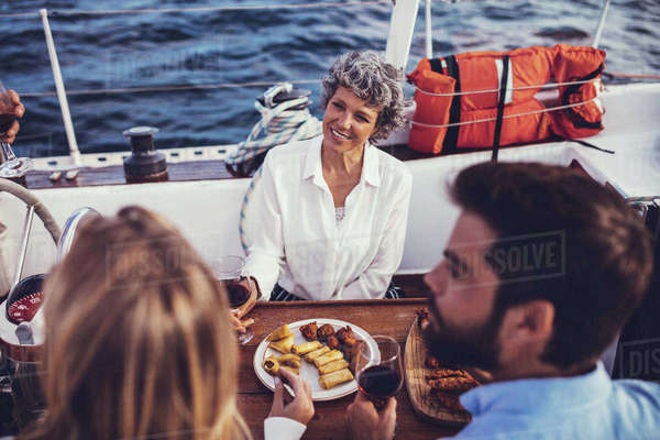 Shot of senior woman with a young couple having meal on the boat ...