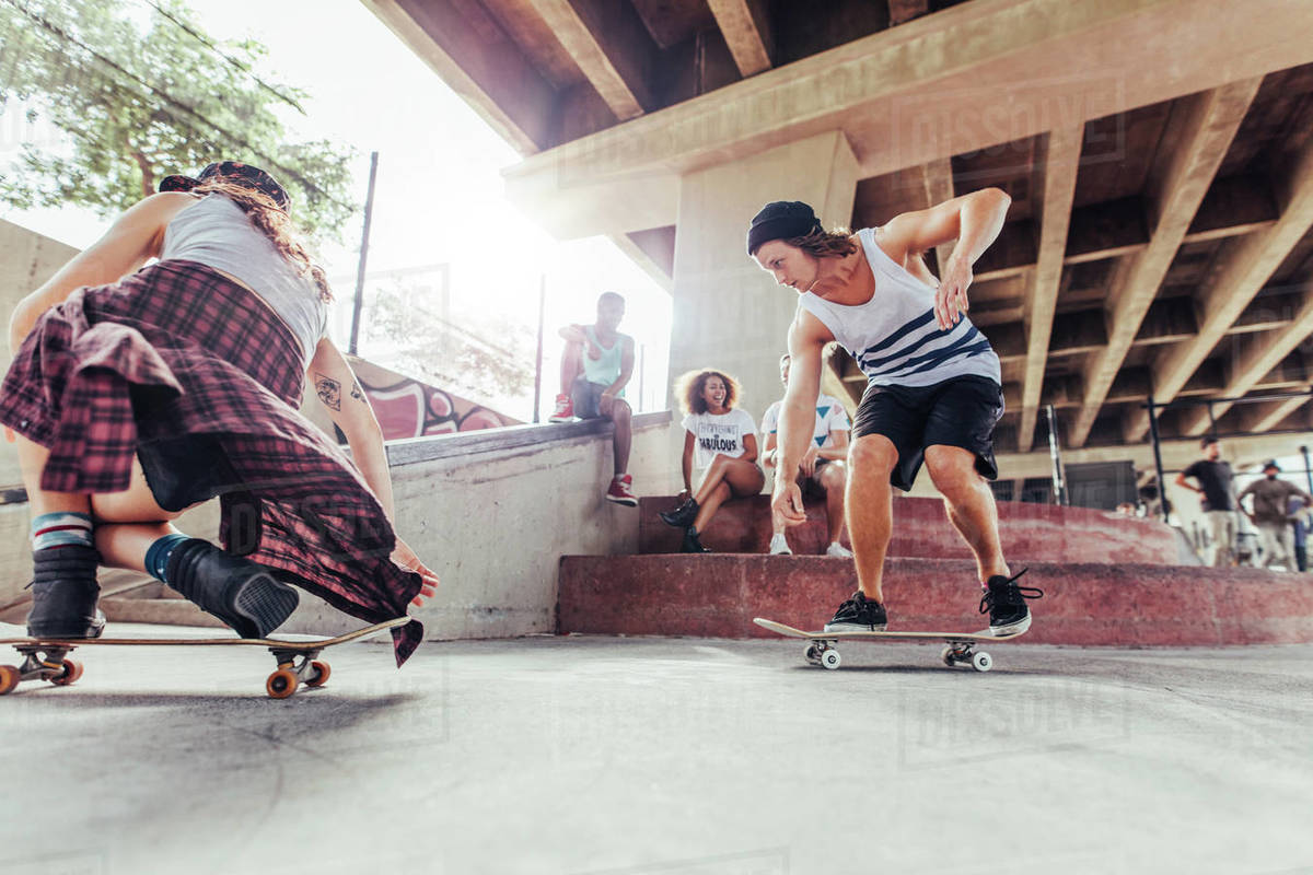 Shot of teenagers skateboarding at skate park with people sitting in ...
