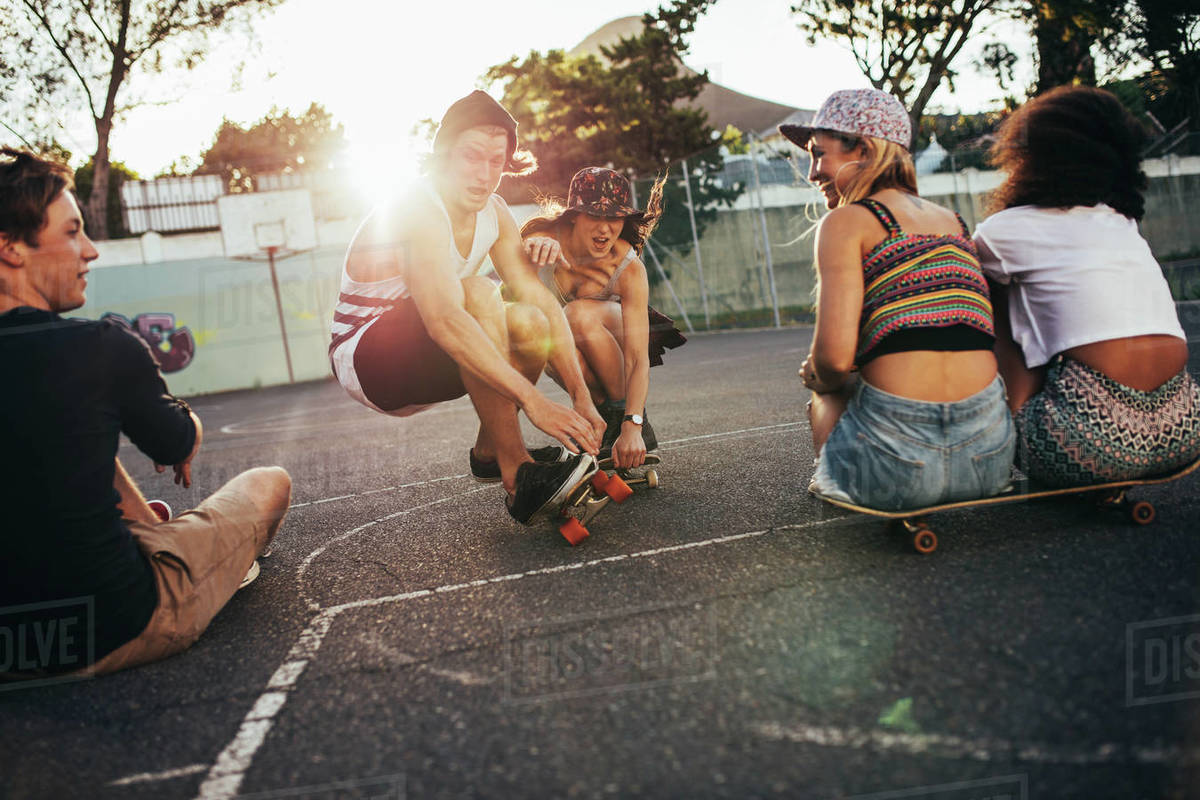 Portrait of young people sitting with two friends skateboarding and ...