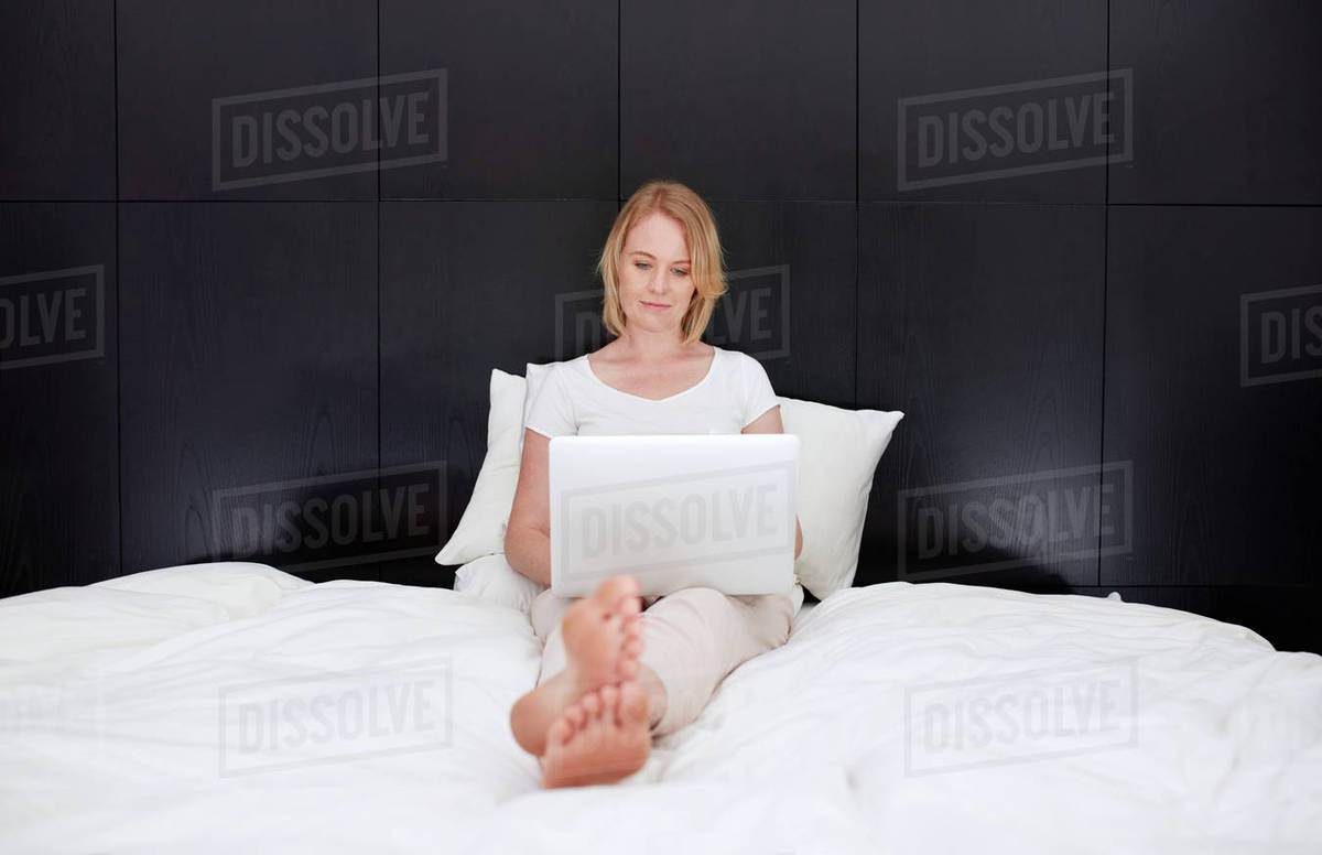 Portrait of a woman sitting on bed and working on her laptop. Caucasian ...