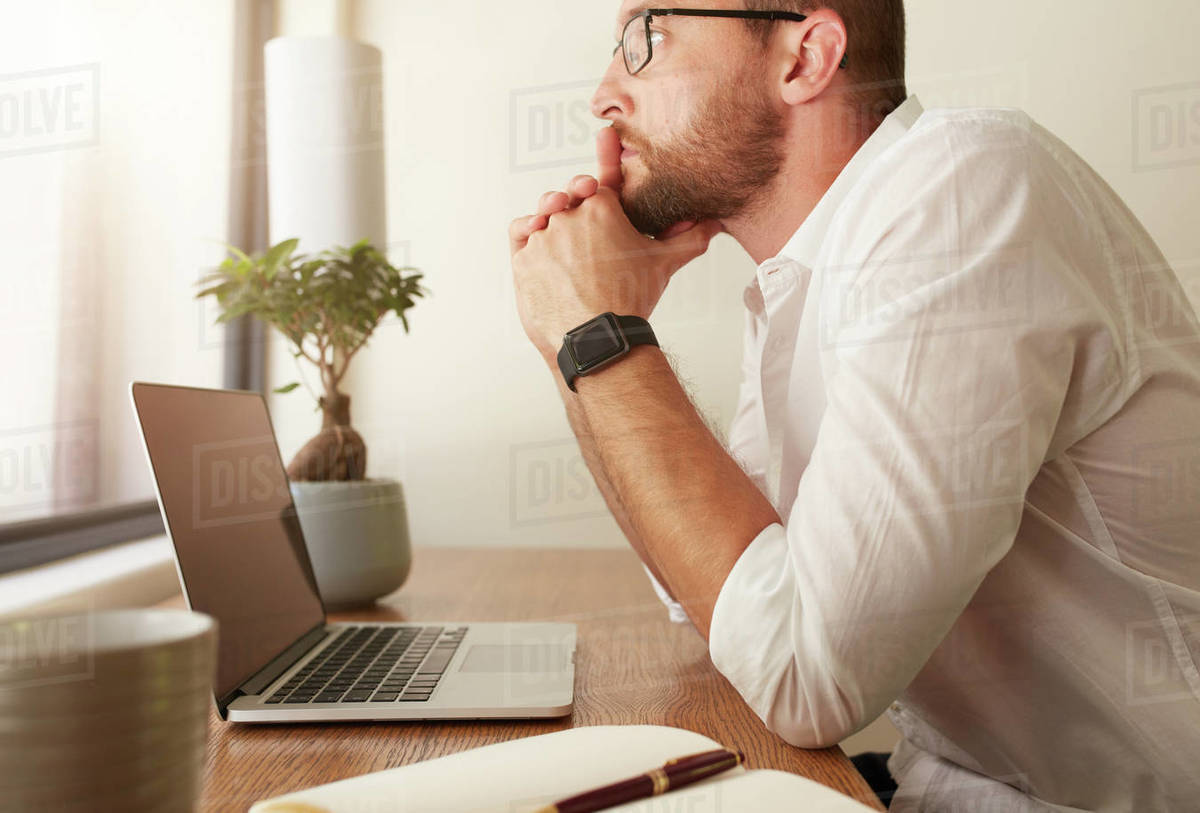 Side view of businessman sitting at his desk with a laptop and looking ...