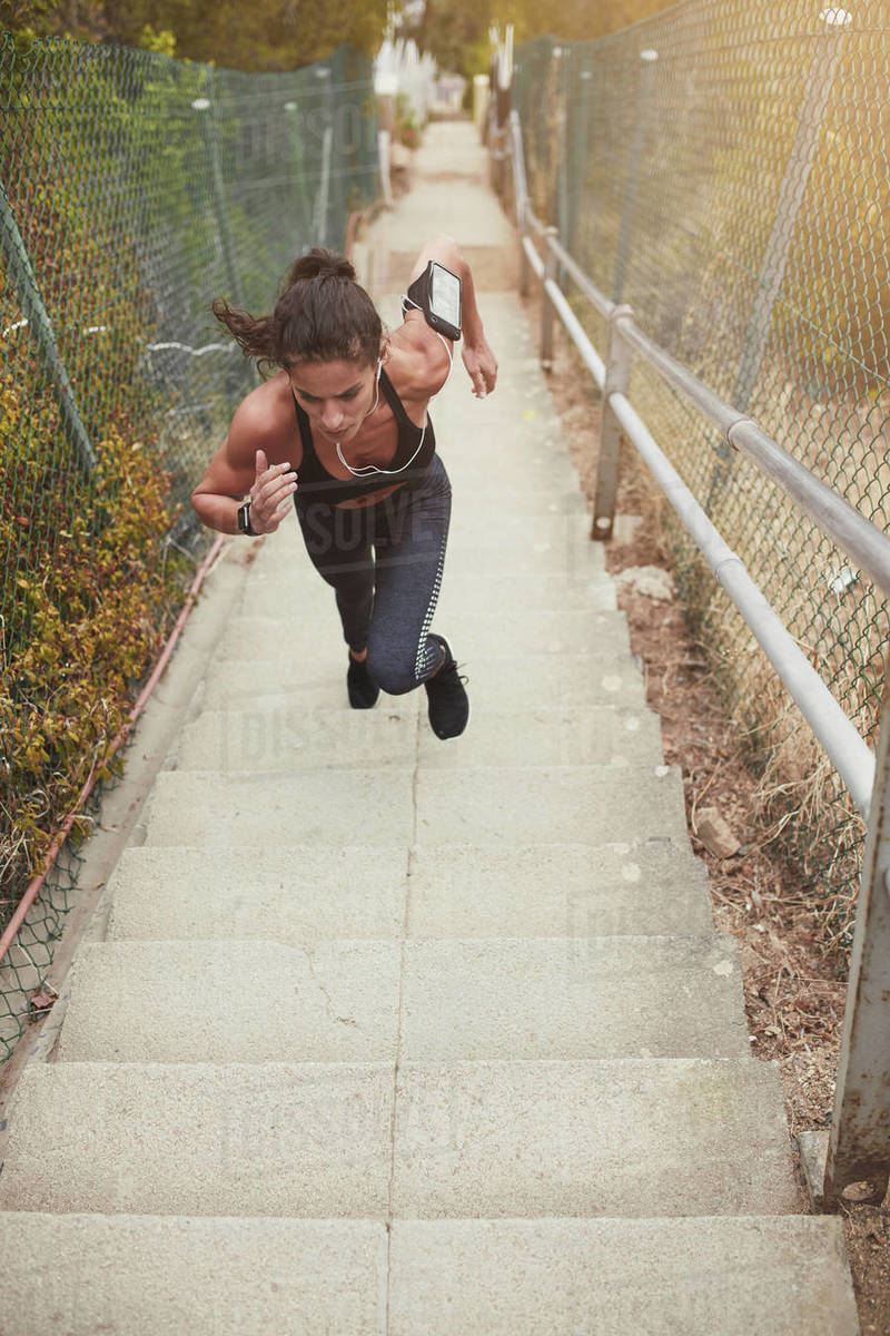Outdoor shot of fit young woman running up stairs. Female athlete ...