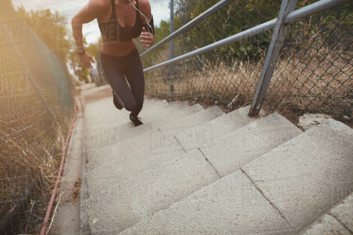 Shot of fitness young woman running up stairs. Female athlete climbing ...