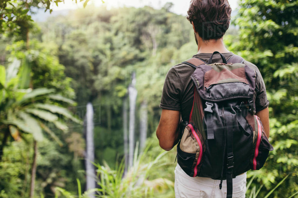 Rear view shot of male hiker with backpack standing on a cliff and ...