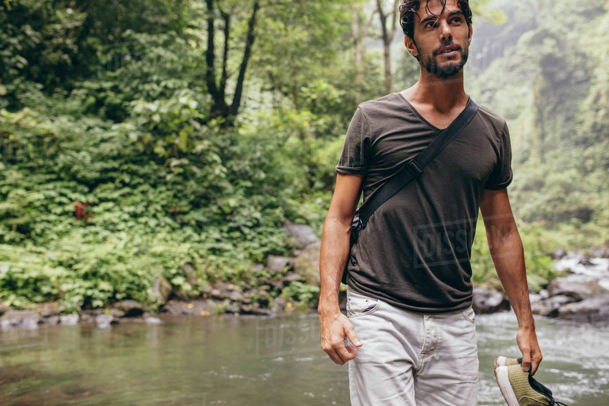 Young man crossing the stream. Caucasian male across the creek on hike ...