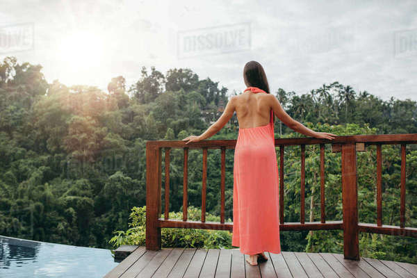 Rear view shot of young woman standing by swimming pool and looking at ...
