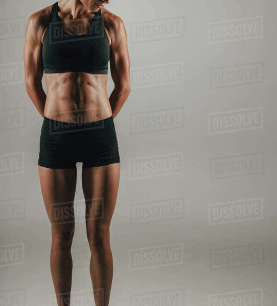 Fit toned strong young woman flexing her abdominal muscles in shadowed ...