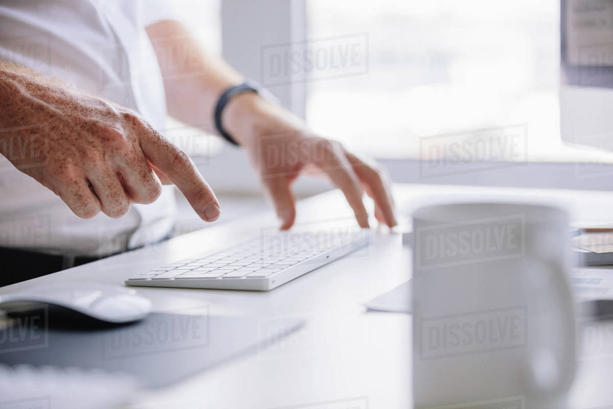 Close up shot of young man hands typing on wireless keyboard on desk in ...