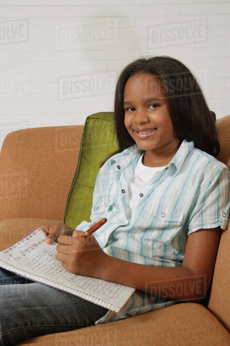 African girl writing in notebook on sofa - Royalty-free Stock Photo ...