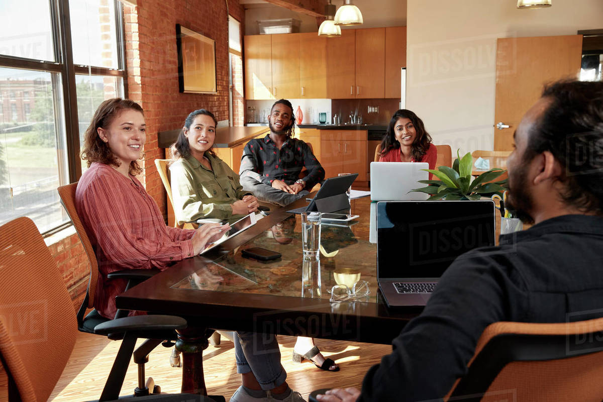 Group of co-workers sitting at large conference table with their ...