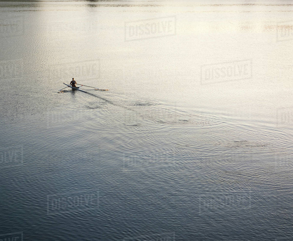 Man rowing single scull rowing boat in calm water and early morning ...
