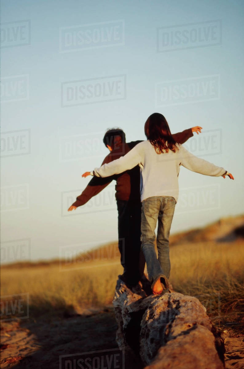 Brother and sister balancing walking along log at beach - Royalty-free ...
