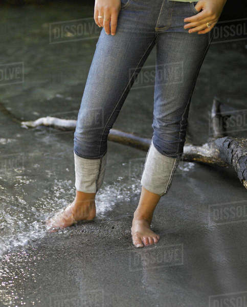 Young woman wearing rolled up jeans and bare feet paddling in water ...