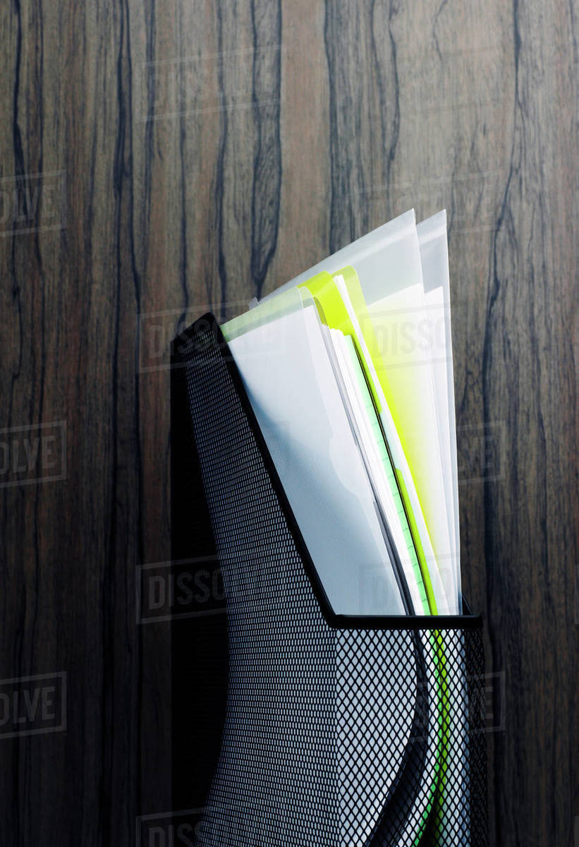 Folders in vertical black metal mesh file holder against wooden ...
