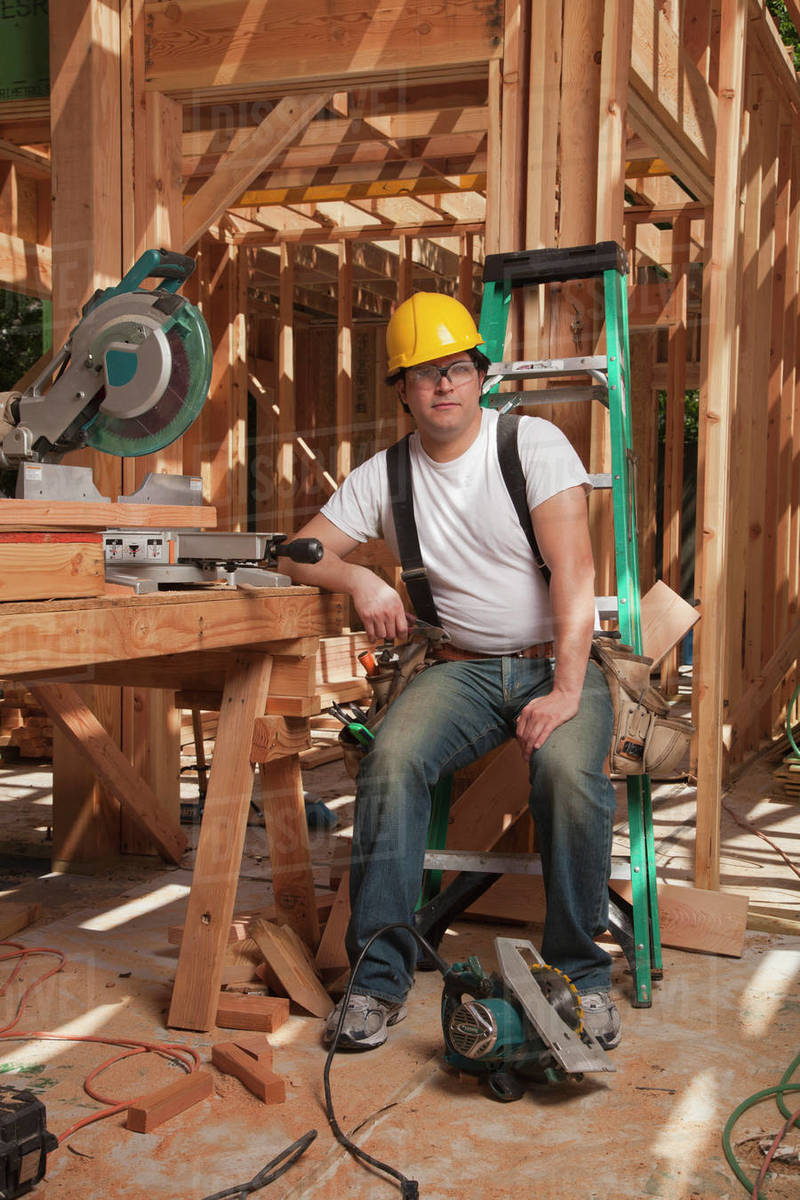 Man at a residential construction site sitting on a ladder and leaning ...