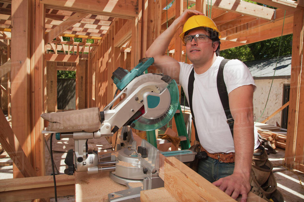 Man wearing a hard hat using a table saw at a residential construction ...