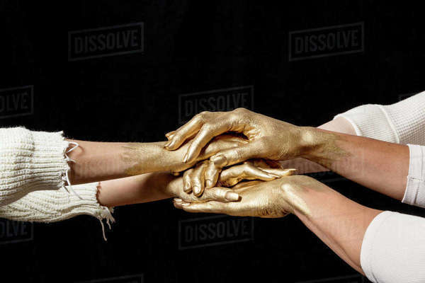 Close-up shot of group's gold painted hands on top of another against ...