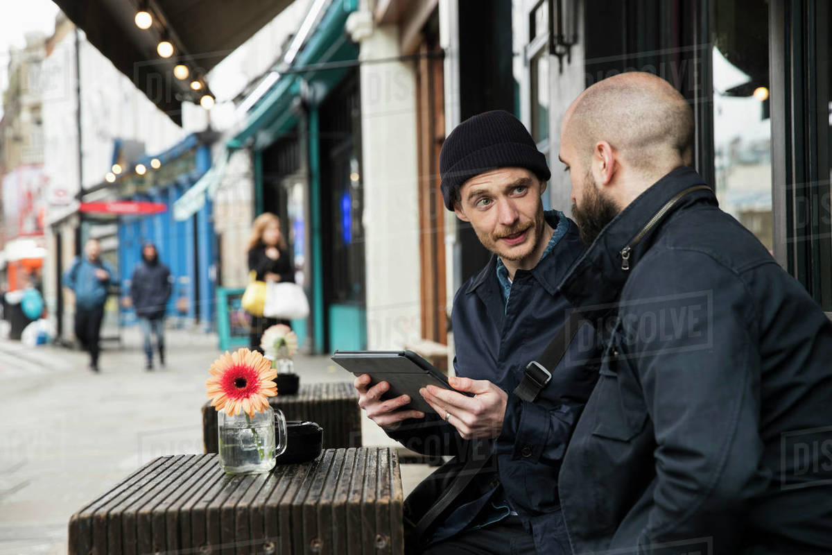 Two men sitting at outdoor cafe table looking at tablet - Royalty-free ...