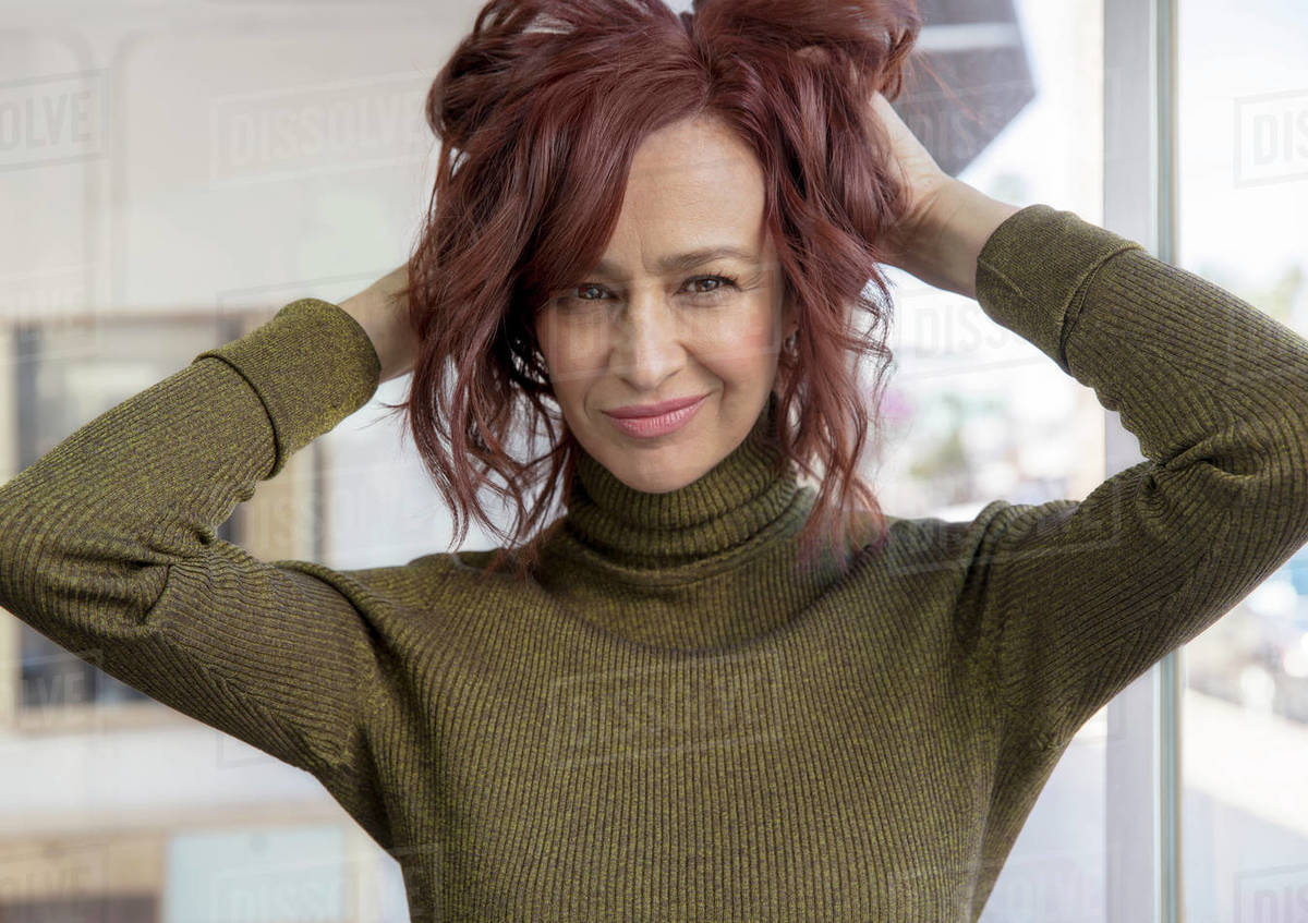 Portrait of a middle-aged woman looking into camera with both her hands up in her hair ...