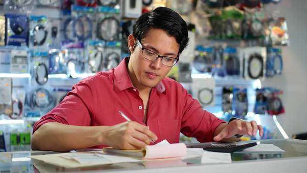Young owner of a computer shop checking bills and invoice with ...