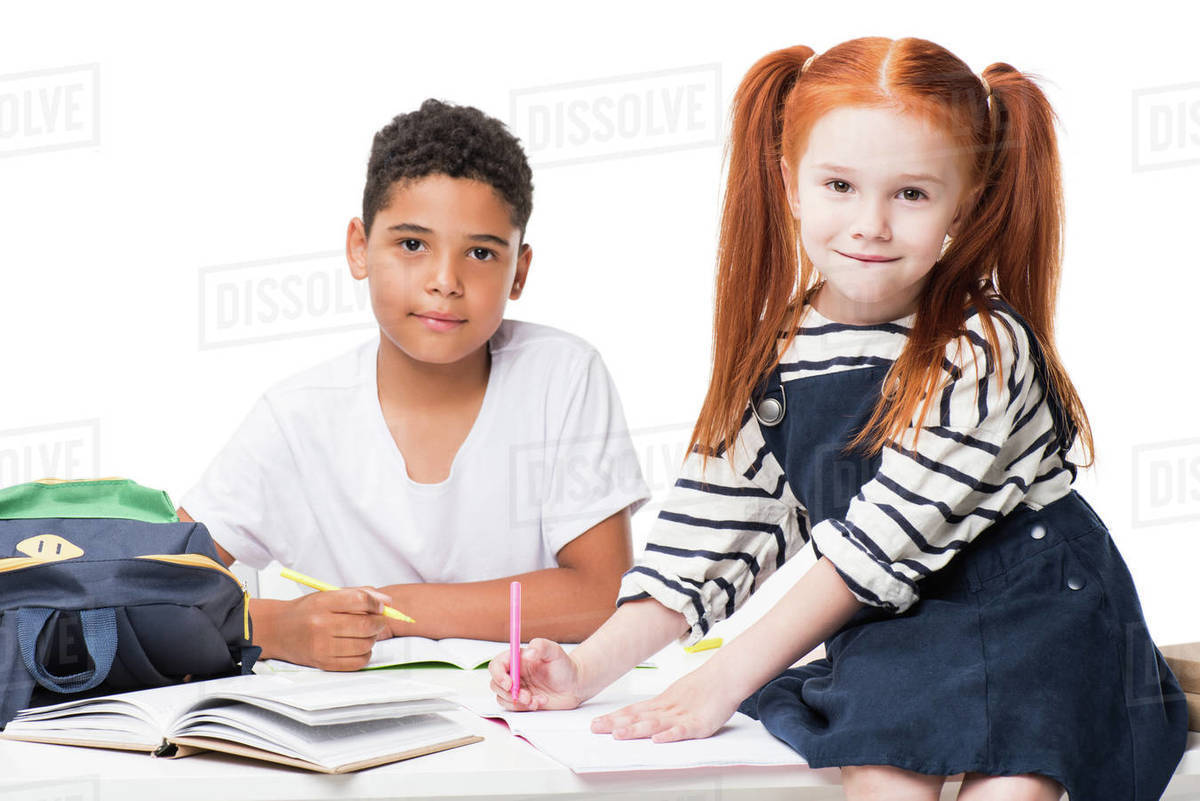 Happy multiethnic schoolkids studying together and looking at camera ...