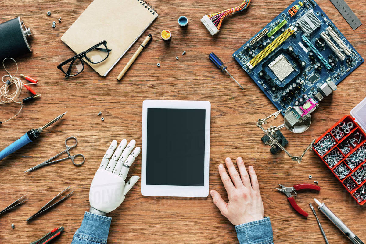 Cropped image of electronic engineer with robotic hand sitting at table ...