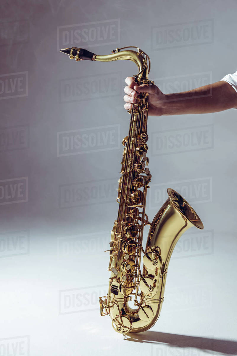 Close-up partial view of man holding saxophone in smoke on grey ...