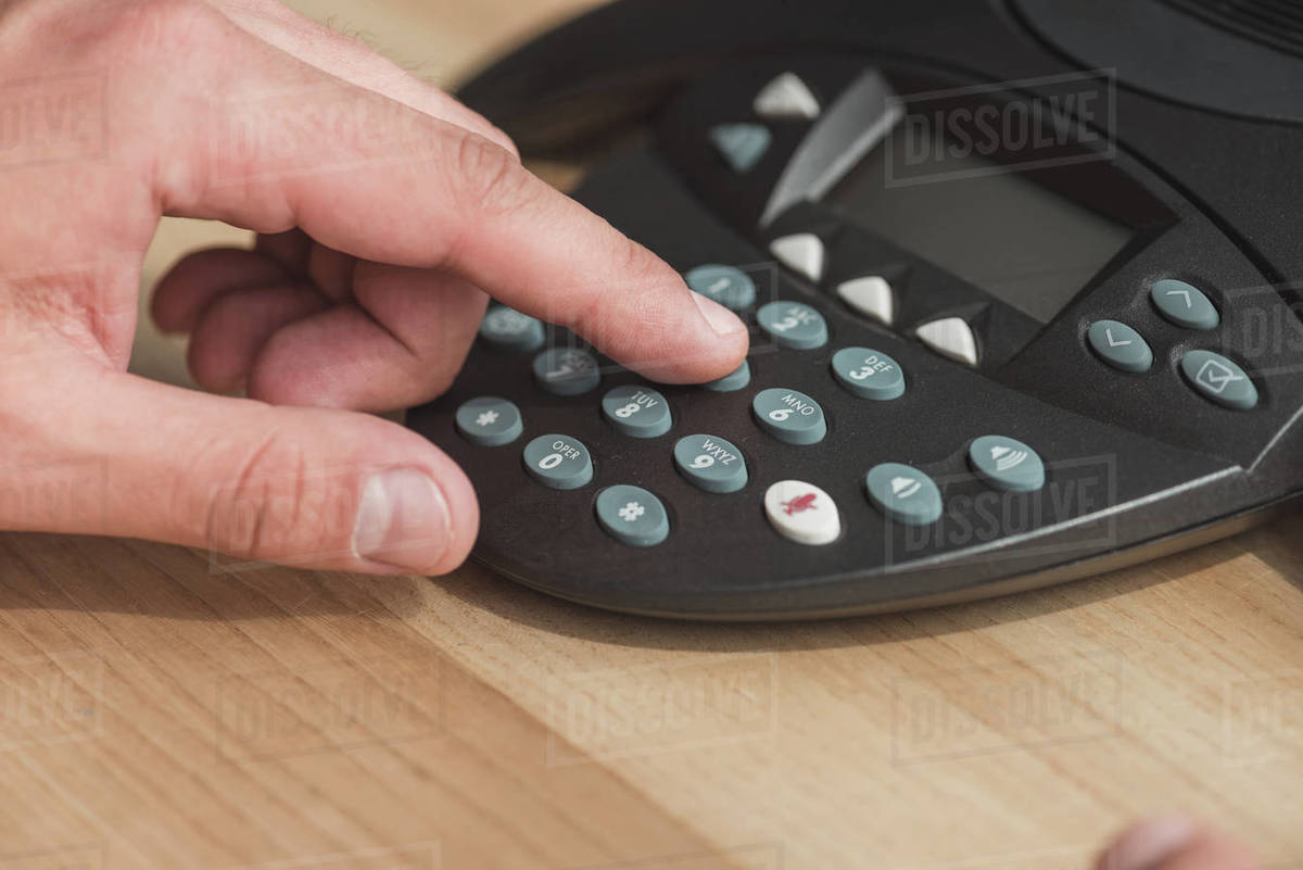 Cropped shot of man pushing button of conference phone on wooden table ...