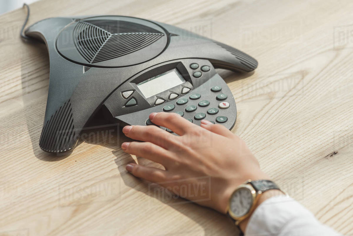 Cropped shot of businesswoman pushing button of speakerphone on wooden ...