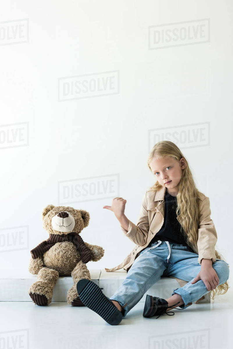 Full length view of beautiful stylish kid pointing at teddy bear and ...