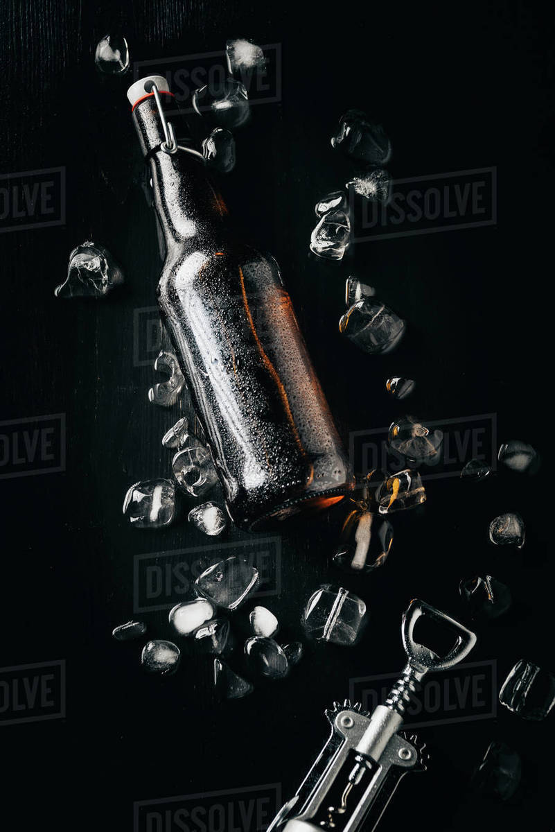 flat lay with bottle opener, bottle of beer on ice cubes arranged on ...