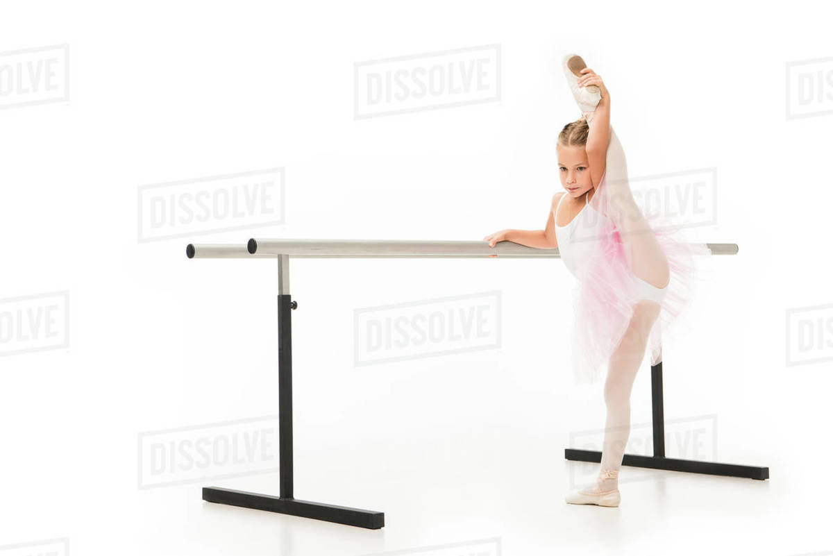 Little ballerina in tutu stretching leg at ballet barre stand isolated ...